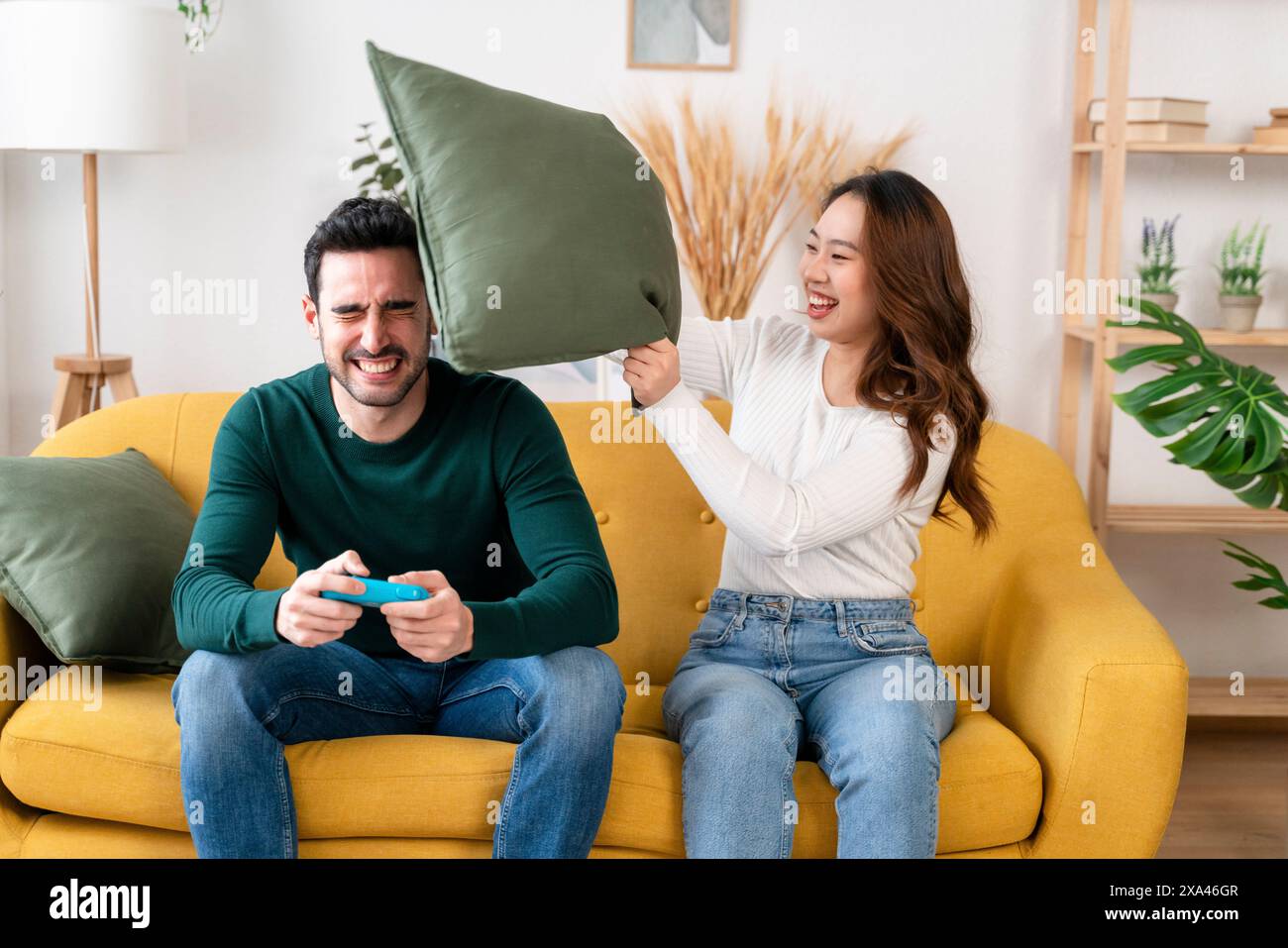 Woman hitting man with pillow as he plays video game Stock Photo - Alamy