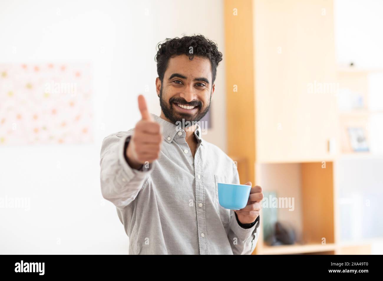 A smiling man with a beard is holding a blue cup in one hand and giving ...