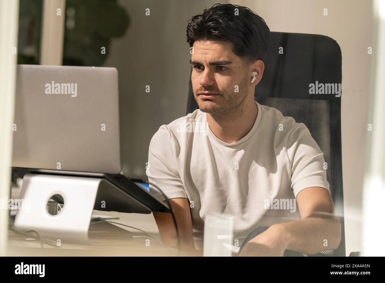 A man sits at a desk behind a computer screen, looking intently at ...