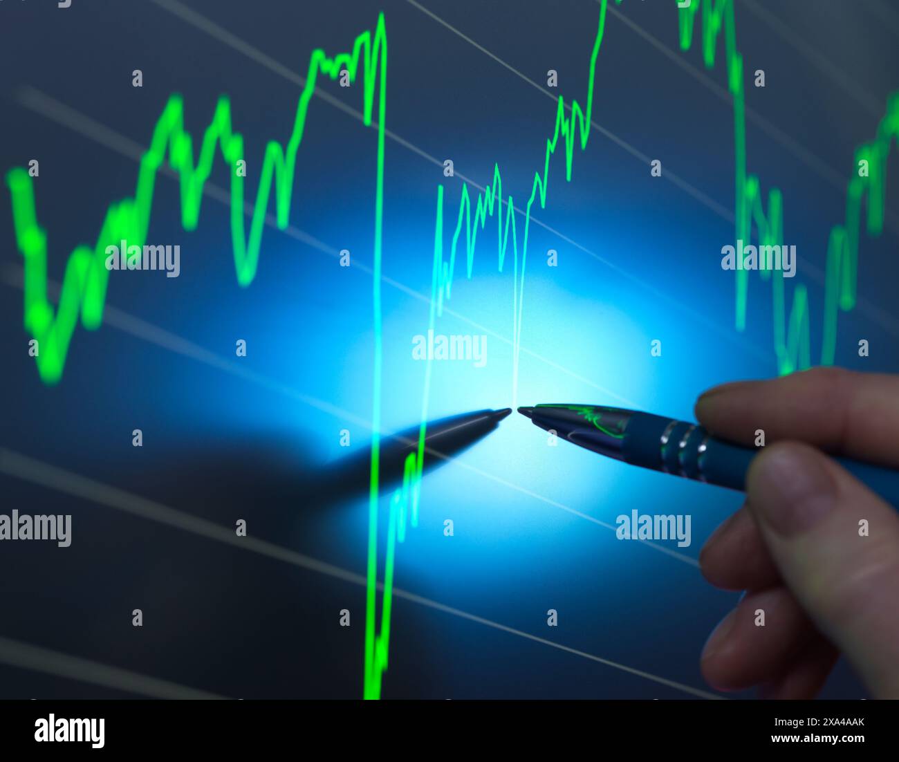 A person's hand holding a pen points to a peak in a glowing stock ...