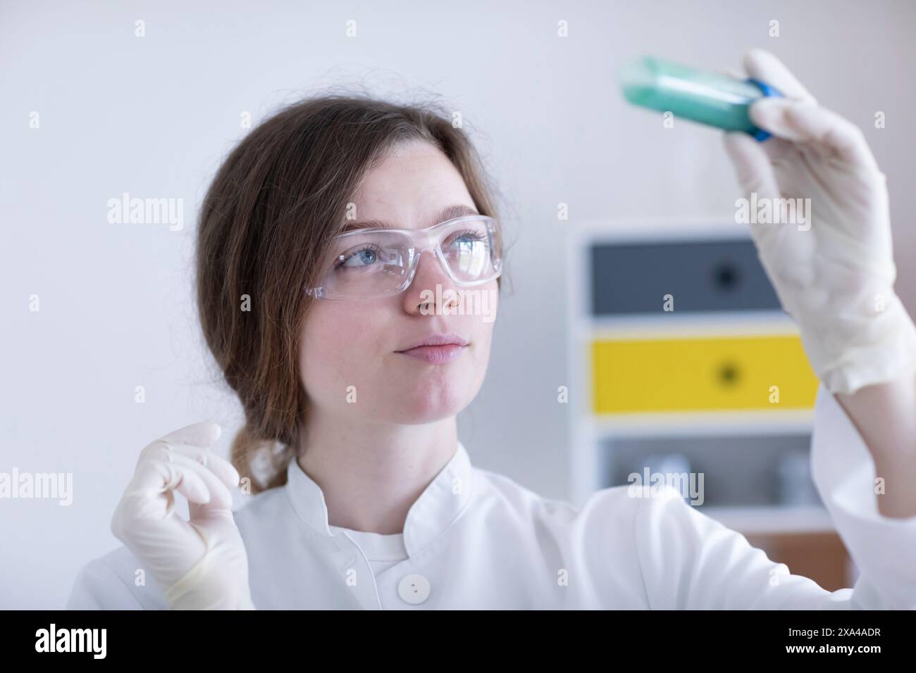 A focused scientist in a lab coat examines the contents of a test tube ...