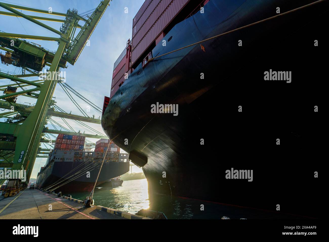 A massive container ship is docked at a port with cranes overhead ...