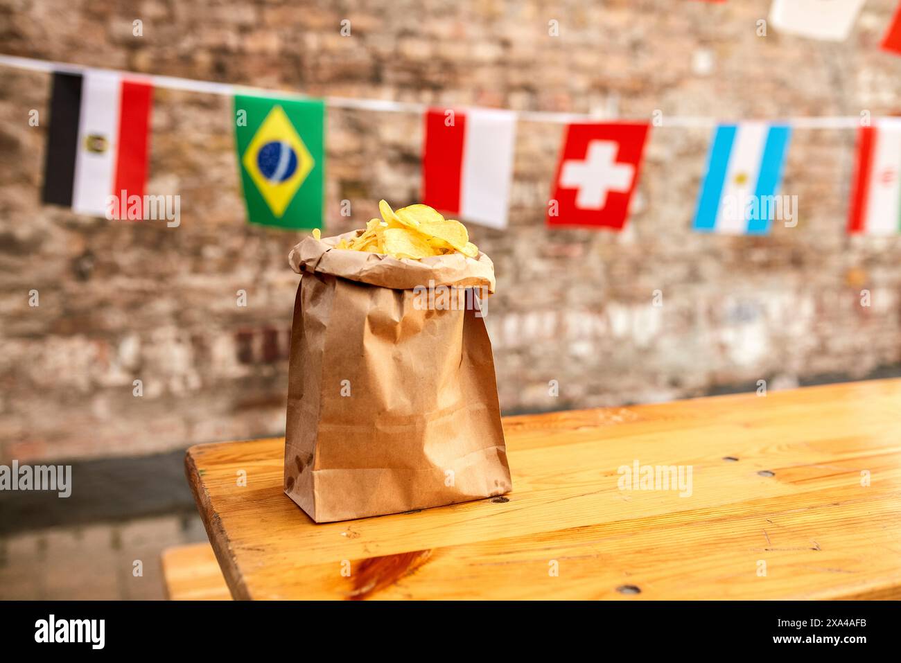 A paper bag filled with potato chips is placed on a wooden table with ...