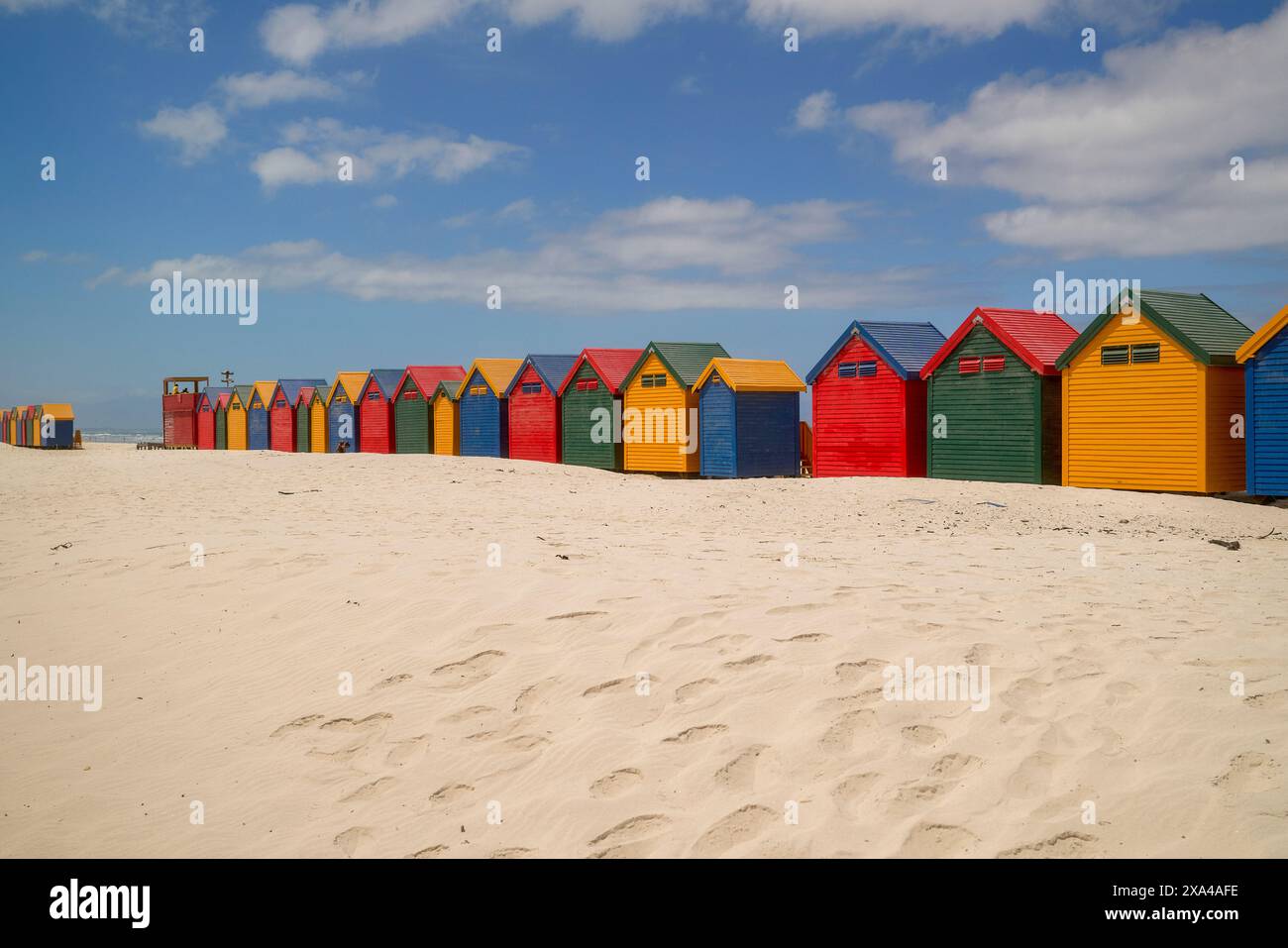 A row of colorful beach huts stands on a sandy beach under a clear blue ...