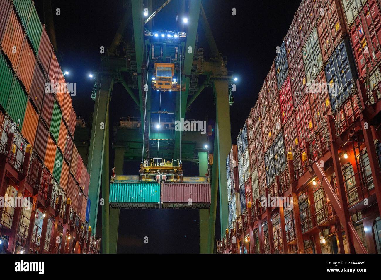 Gantry crane moving container amidst stacked multicolored containers hi ...