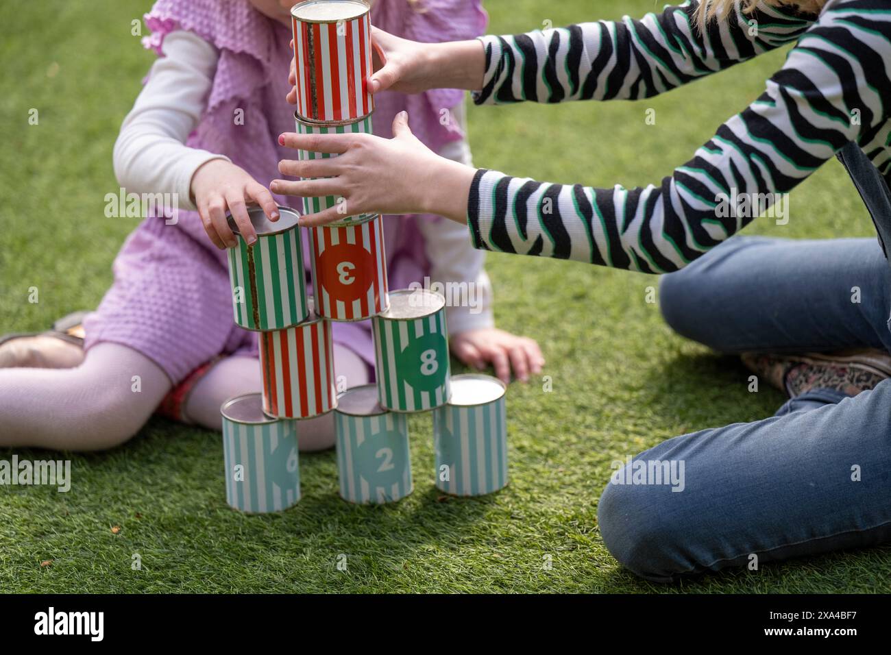 Two children are playing with colorful numbered cans on a grassy ...