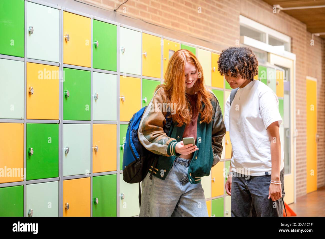 Two teenagers are standing in a hallway by a row of colorful lockers ...