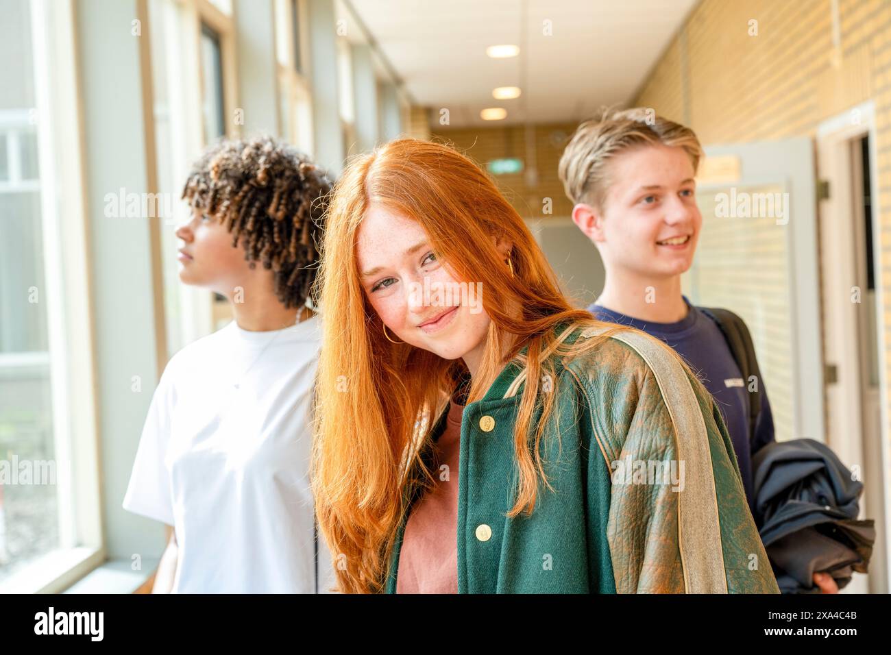 Three students standing in a school corridor, smiling and posing for ...