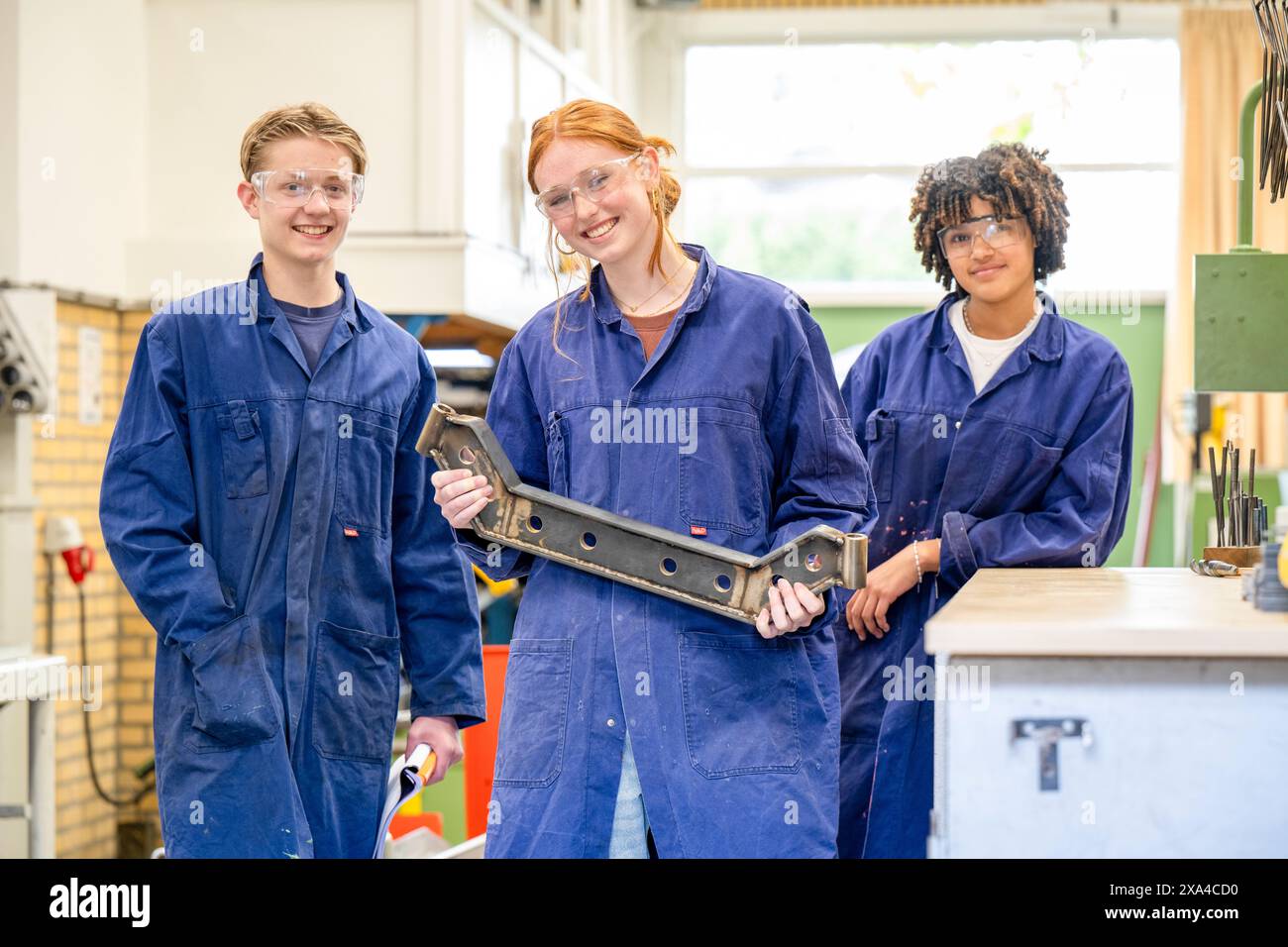 Three apprentices stand side by side dressed in blue work overalls in a ...