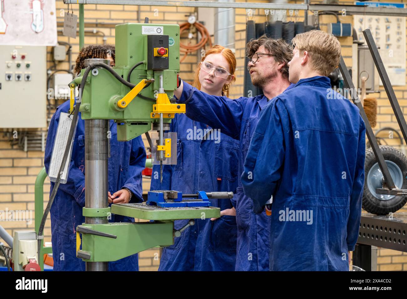 Three people wearing blue work coveralls are attentively observing a ...