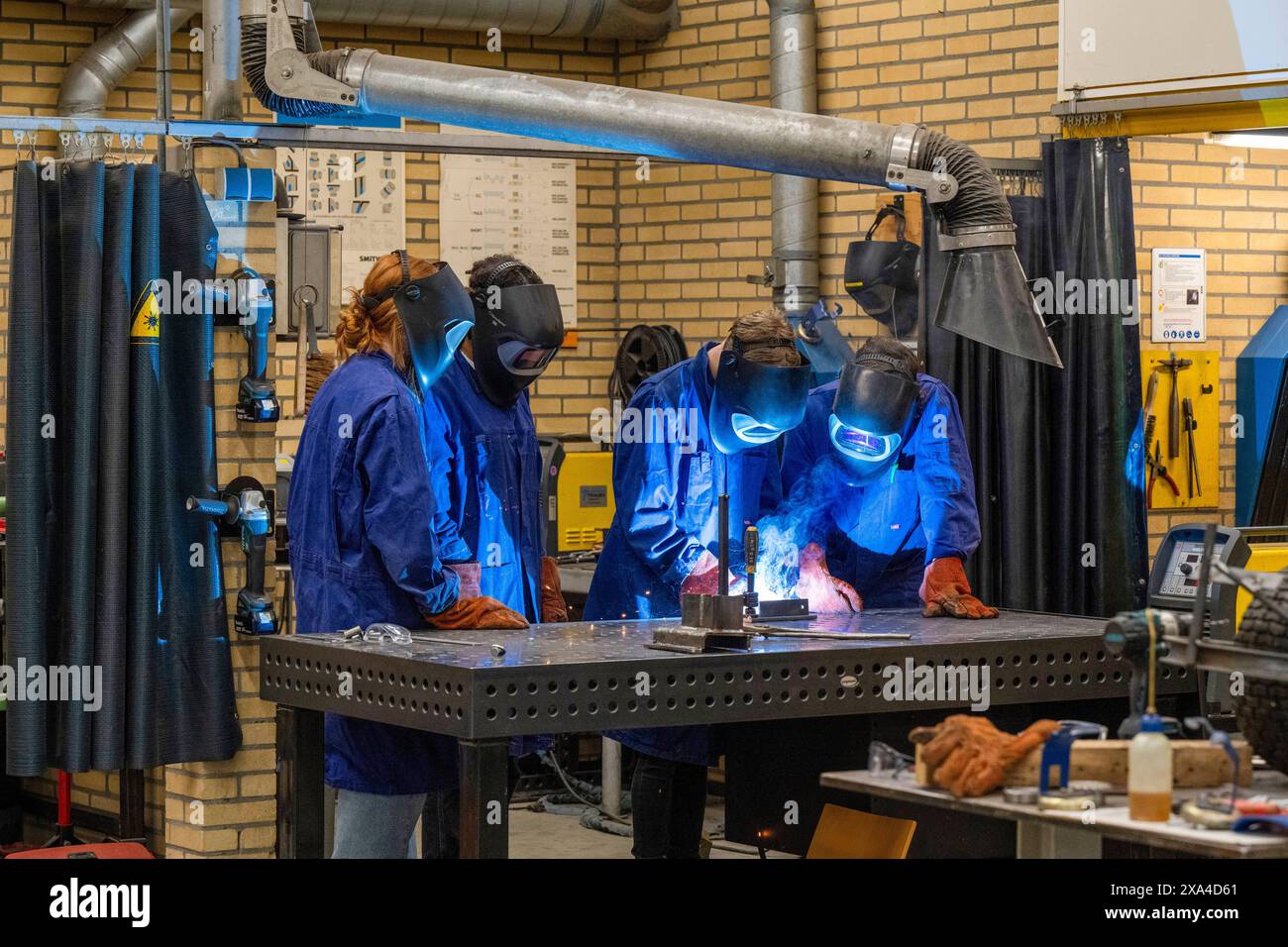 Three individuals are engaged in welding activity in a workshop setting ...
