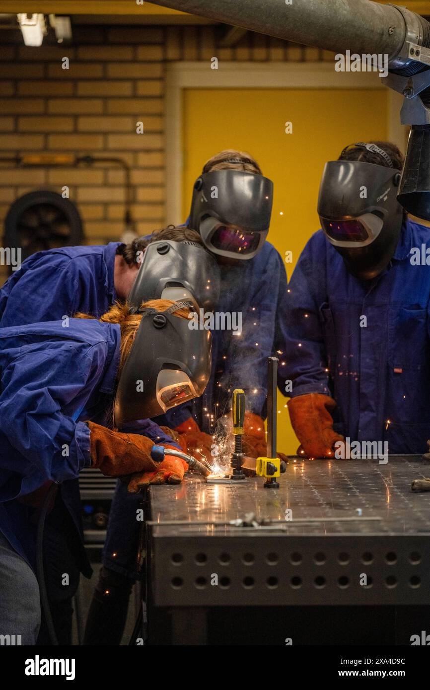 Three people are engaged in welding work at a workshop, wearing ...