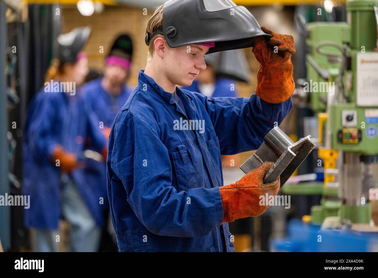 A worker in blue overalls and safety gloves inspects a metal part while ...