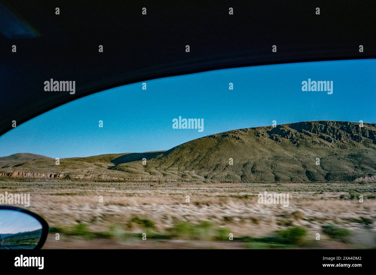 A view of a barren hillside from a moving car with the window frame ...