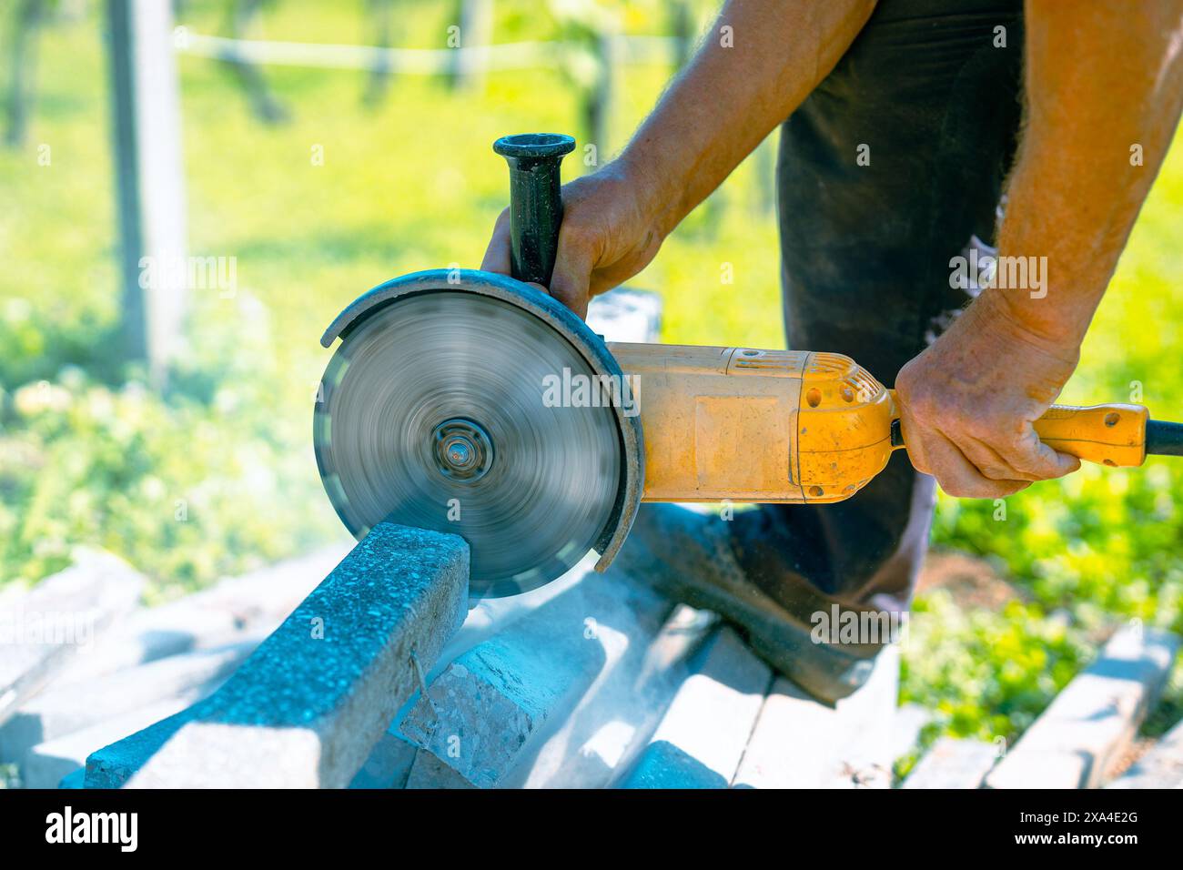Person using big yellow grinder to cut concrete poles in home garden ...