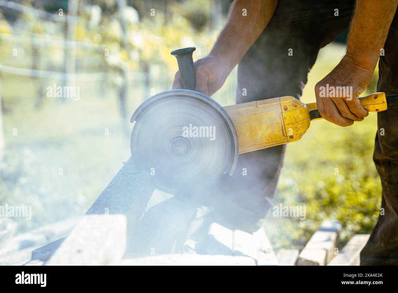 Person using big yellow grinder to cut concrete poles in home garden ...