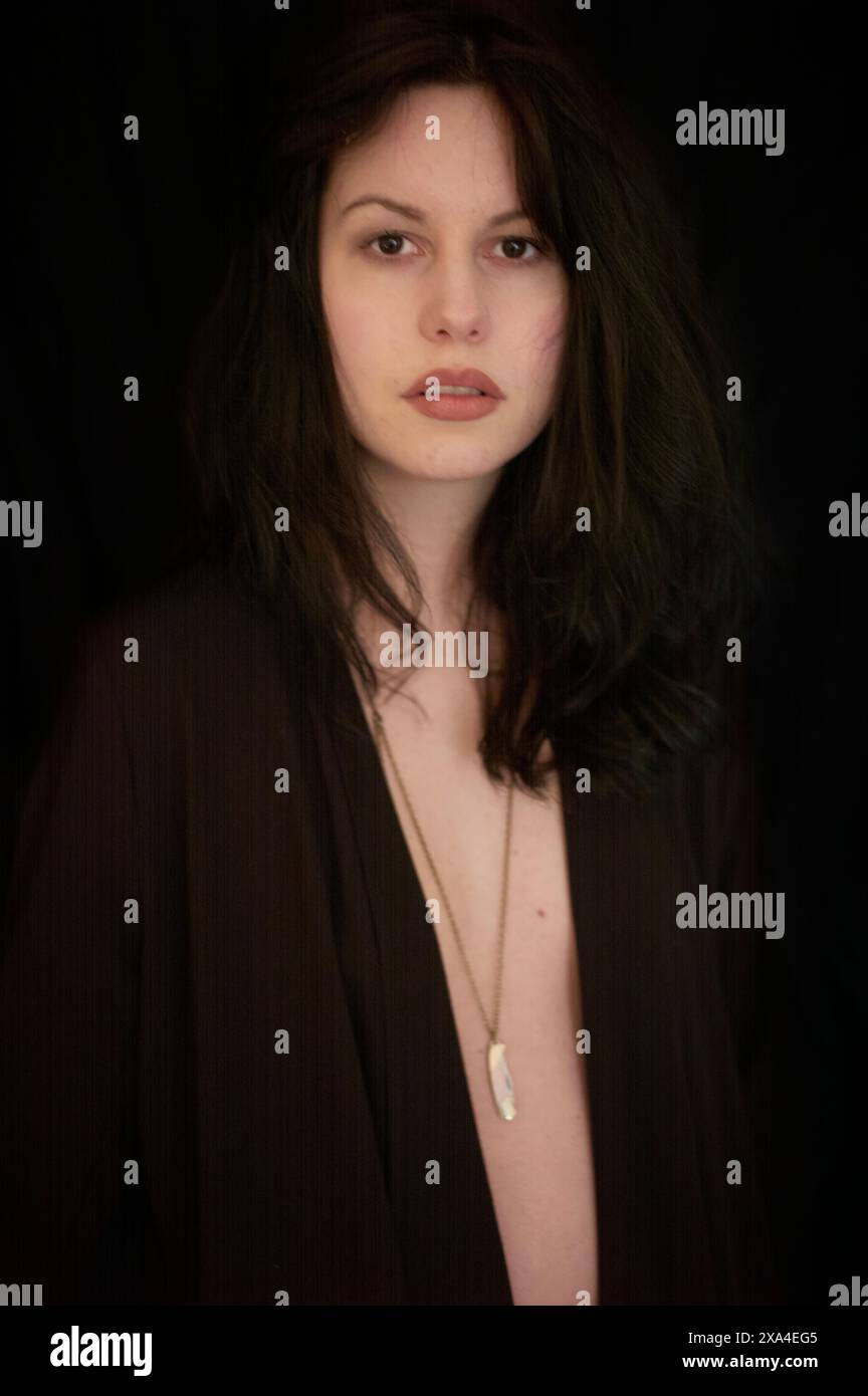 A young woman with disheveled dark hair and a neutral expression is ...