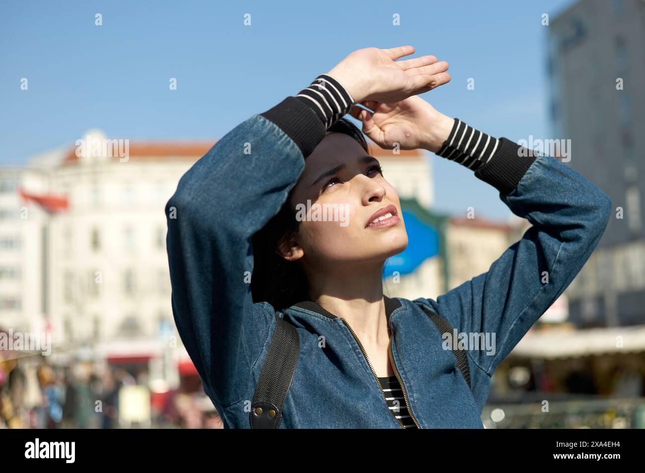 A young woman is outdoors on a sunny day, shading her eyes with her ...