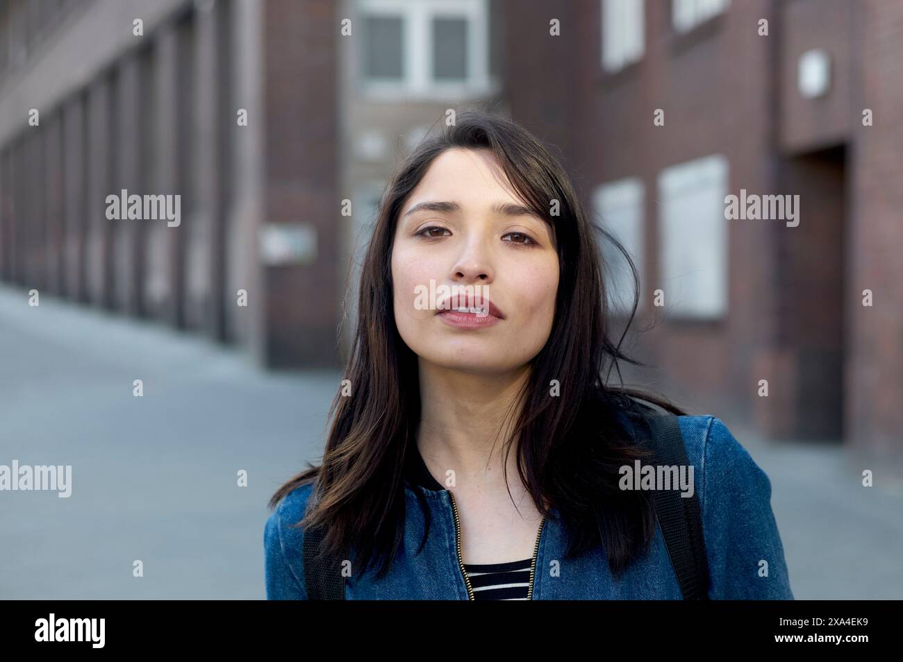 A woman standing in front of a brick building with a focused expression ...