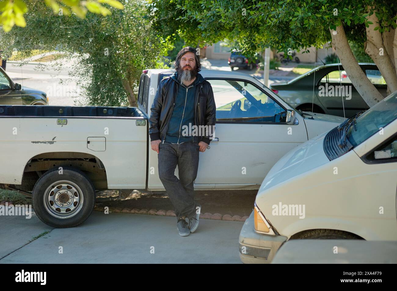 A man stands between two white pickup trucks on a residential street ...