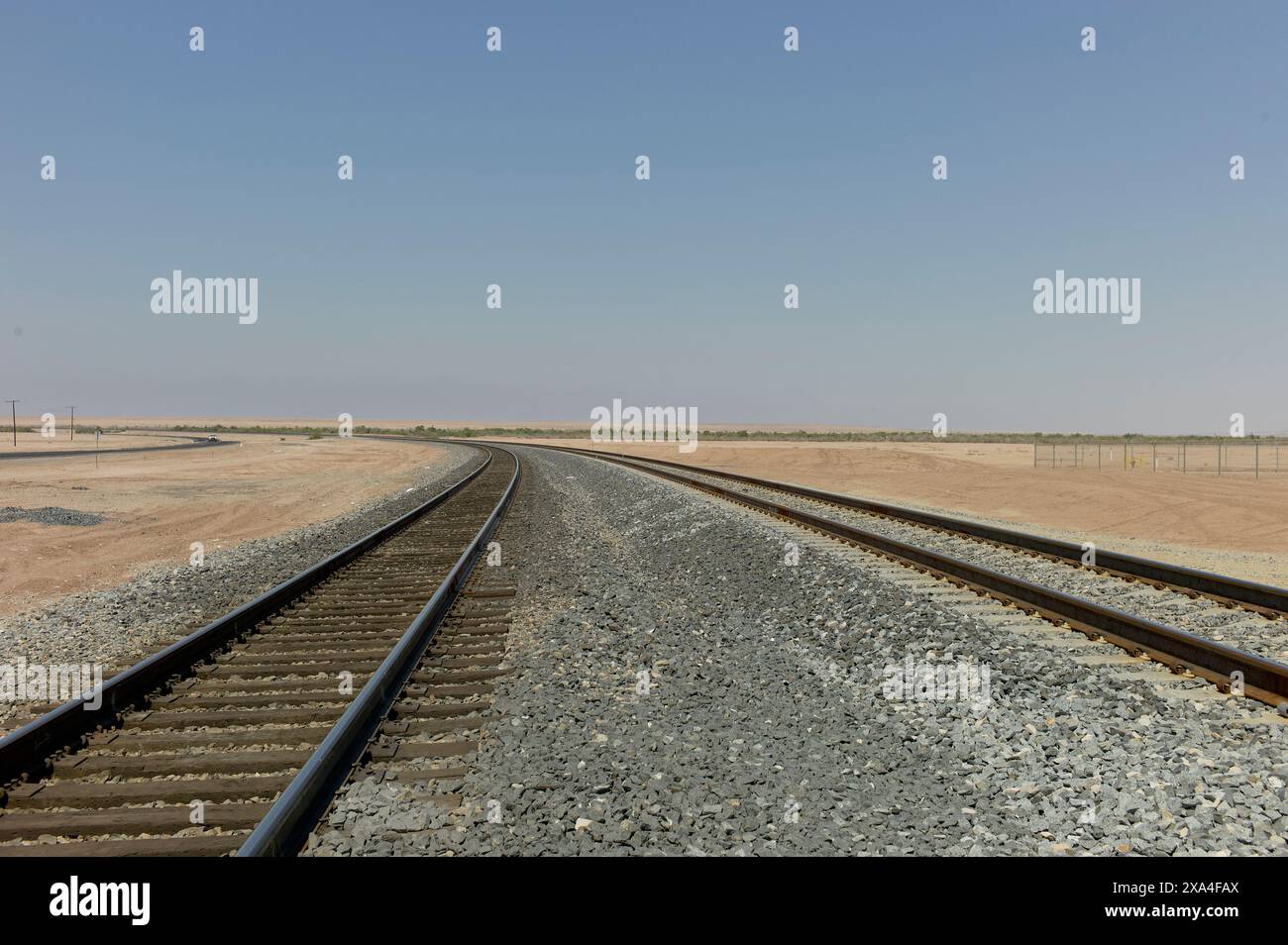 A view of railroad tracks extending straight into the horizon in a desert landscape under a ...
