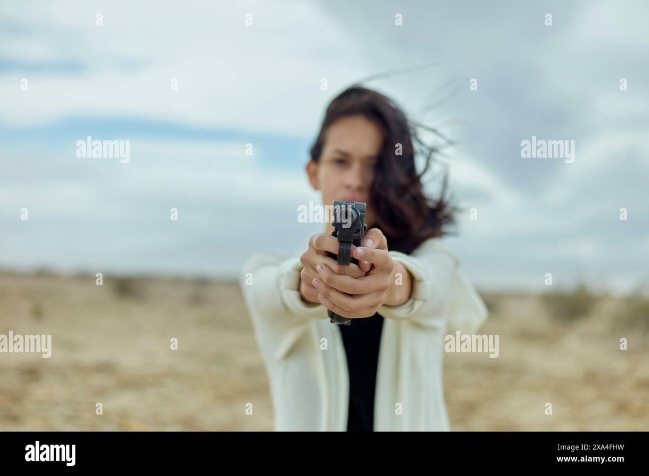 Woman hair blowing wind holding gun aimed forward focused expression hi ...