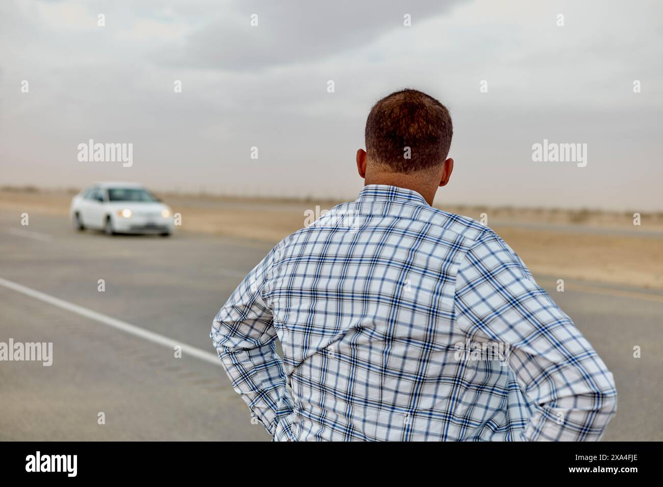 A man is seen from behind watching a car drive away on a deserted road ...