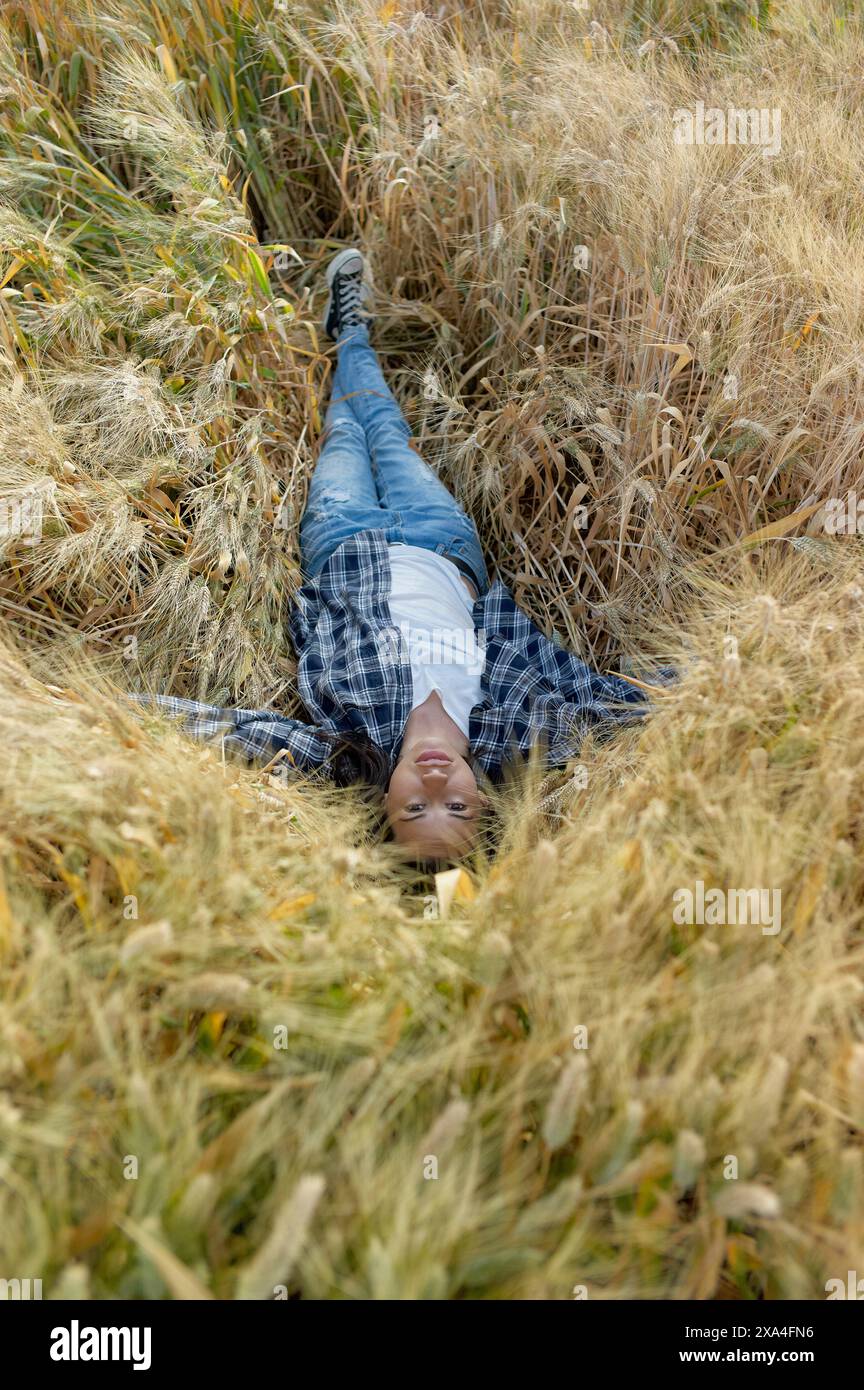 A person is lying in a field of tall golden grass, wearing a checkered ...