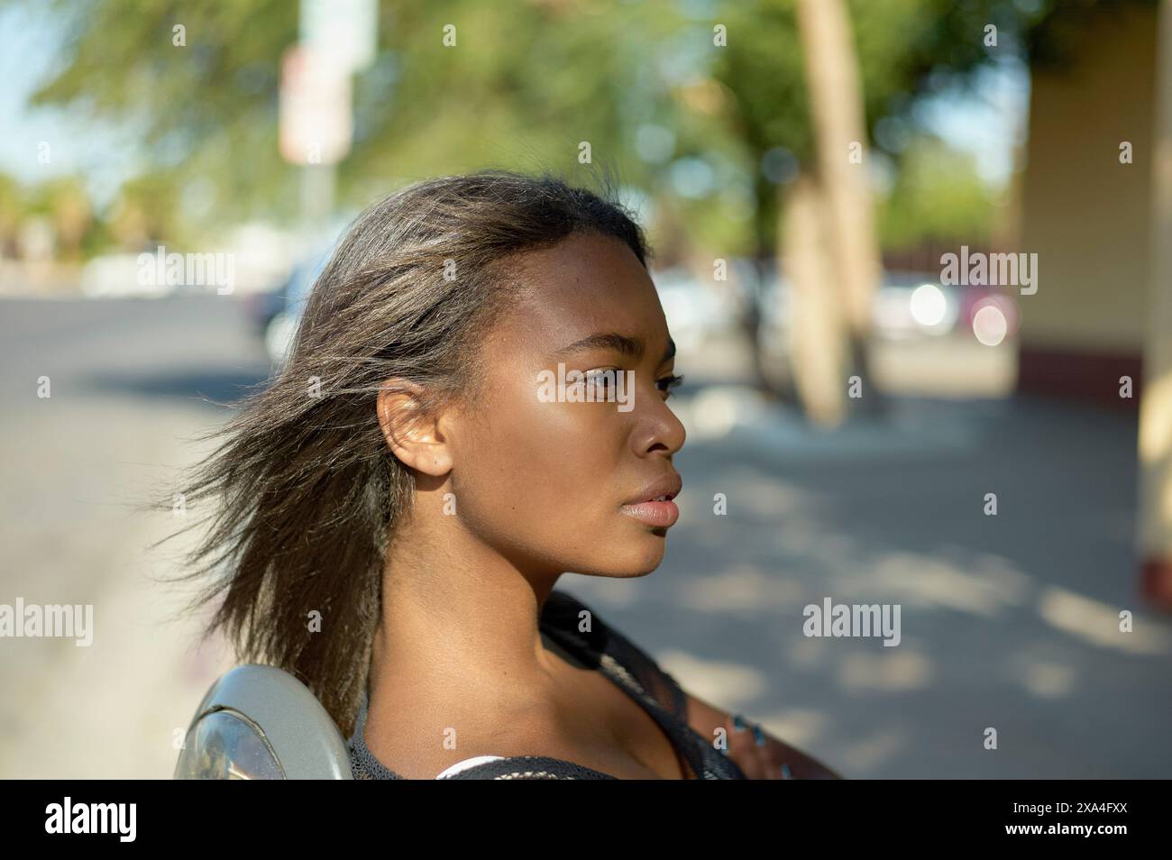 A young woman with her hair fluttering in the breeze stands outdoors ...
