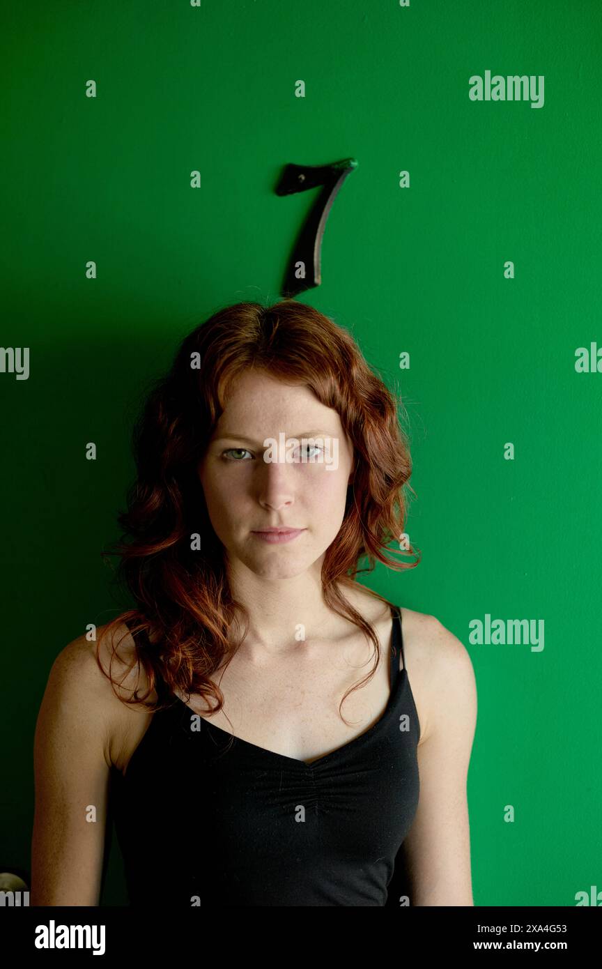 A woman with red hair is standing against a green background with the ...