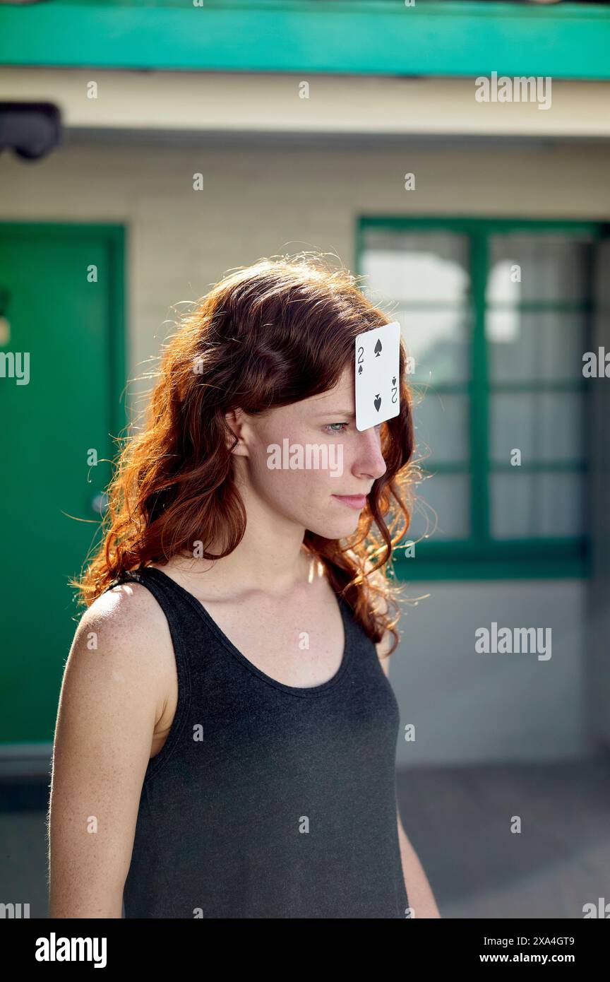 A woman with red hair has an ace of spades card balanced on her ...
