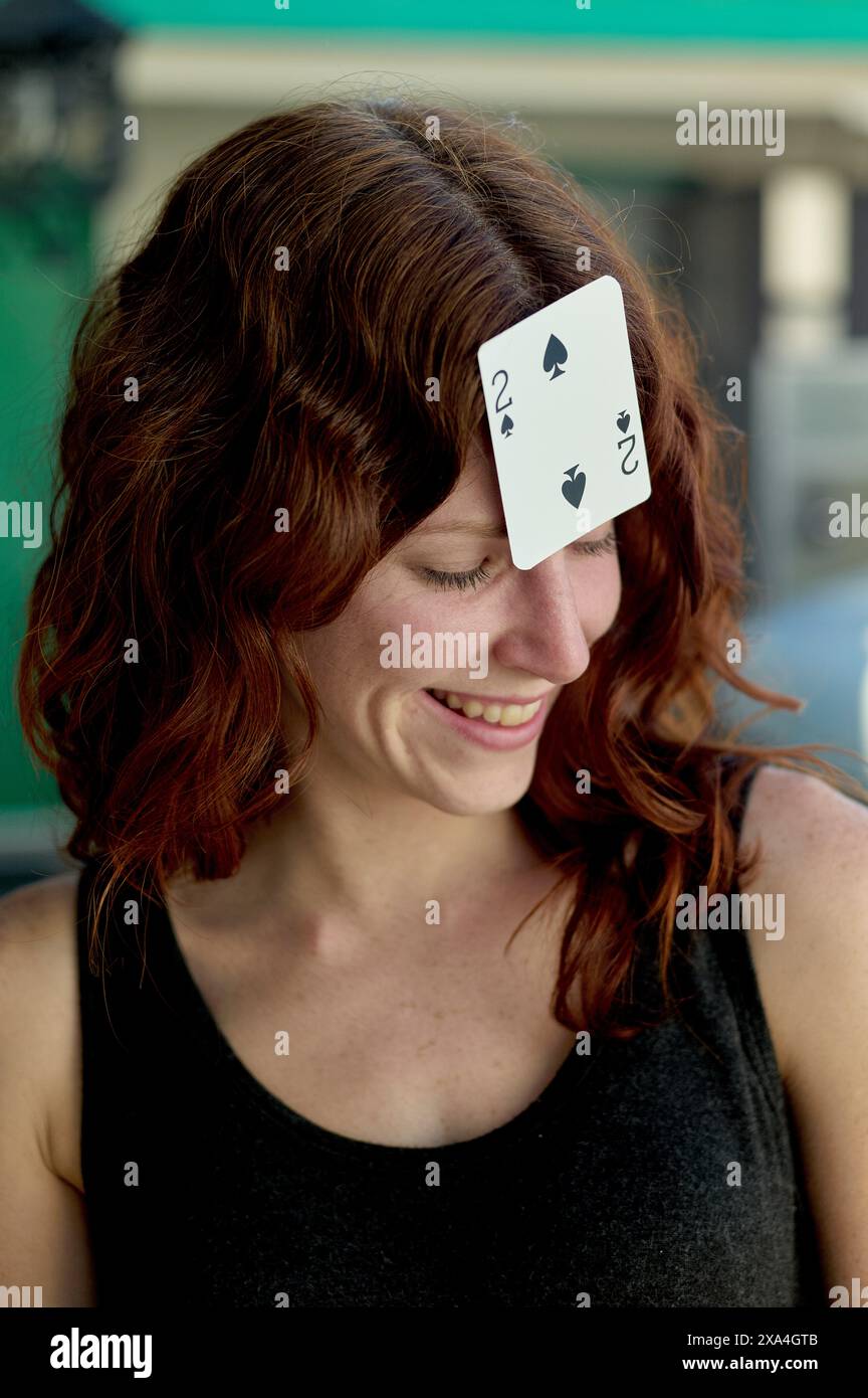 A smiling woman with red hair has a playing card, the two of spades ...