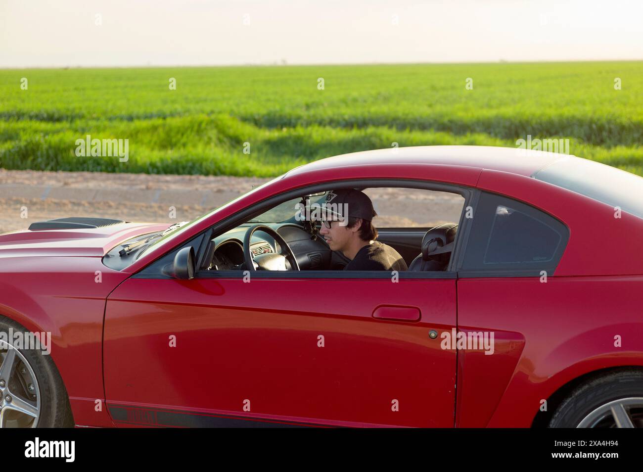 A person wearing sunglasses and a cap is driving a red sports car ...