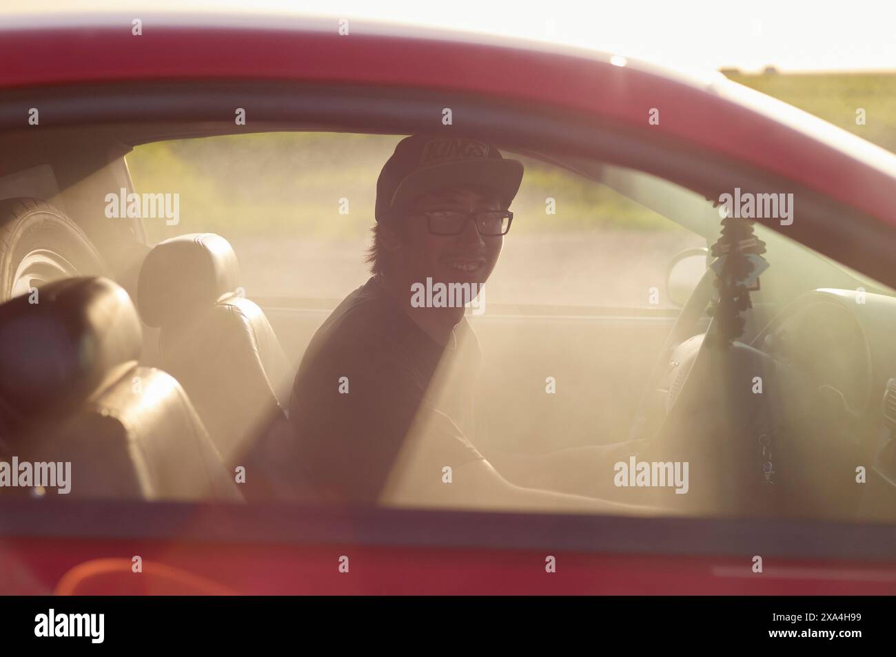 A man wearing a baseball cap and glasses smiles as he sits in the ...