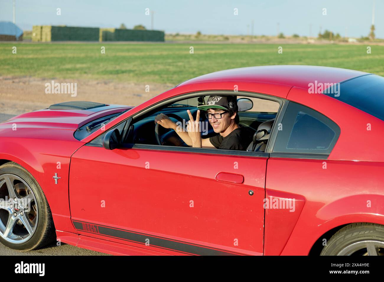 A man smiles while giving a thumbs-up from the driver's seat of a red ...