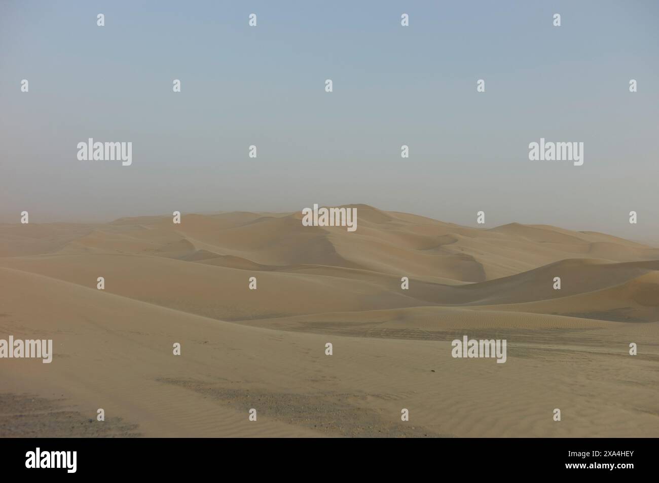 A serene expanse of desert dunes under a hazy sky, with the sand ...