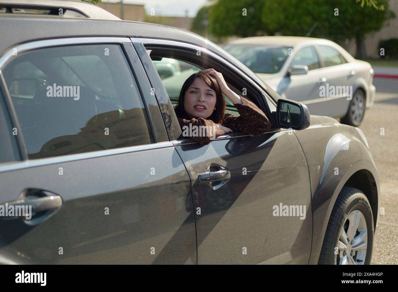 A woman is looking through the open window of a parked car, resting her ...