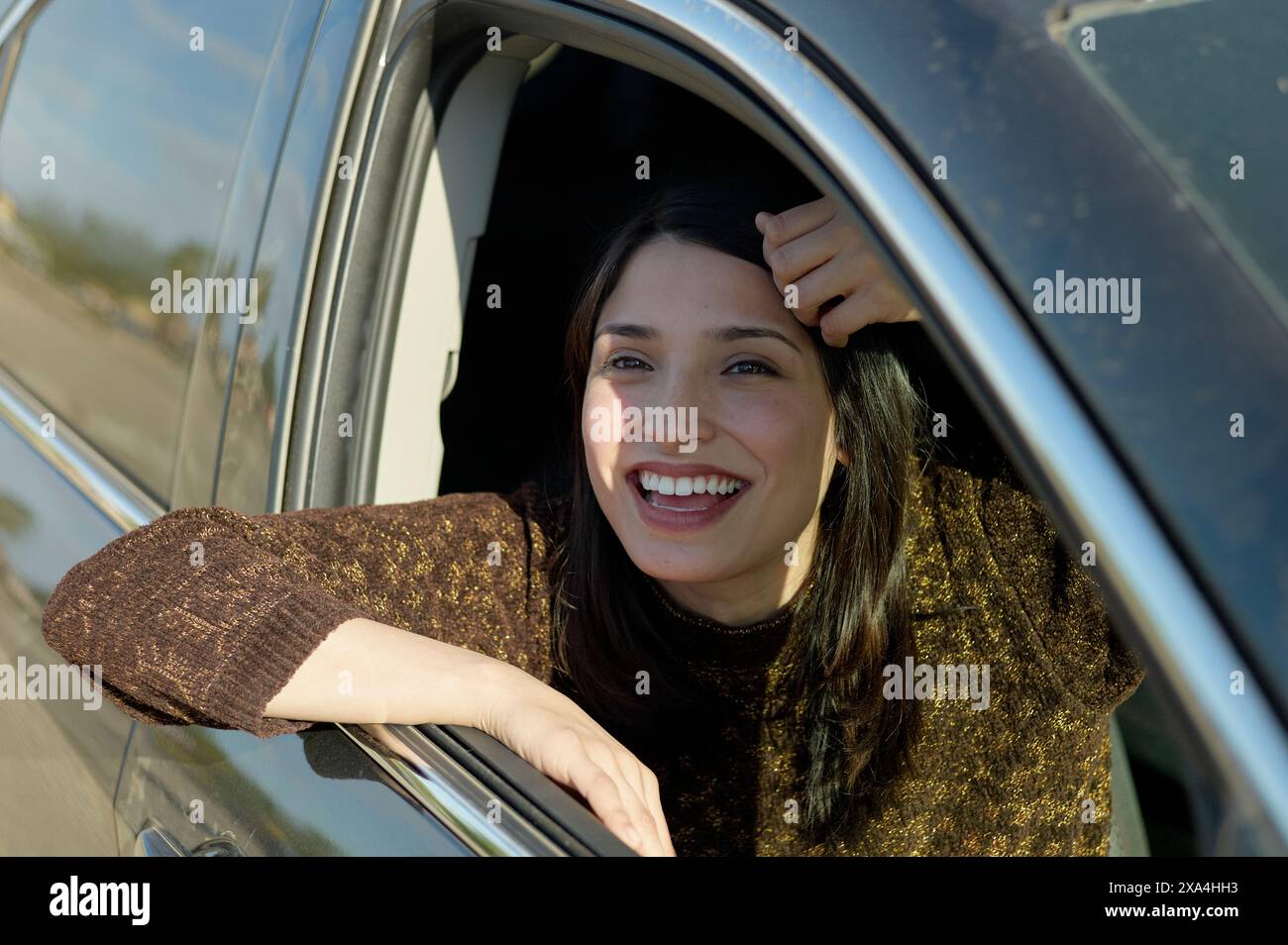 A smiling woman is leaning out of the driver's side window of a car ...