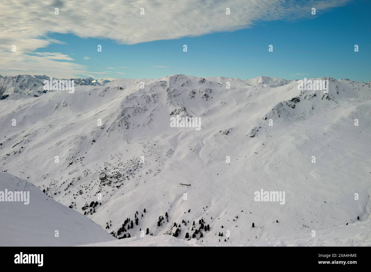 A vast snow-covered mountain range under a clear blue sky with shadows ...