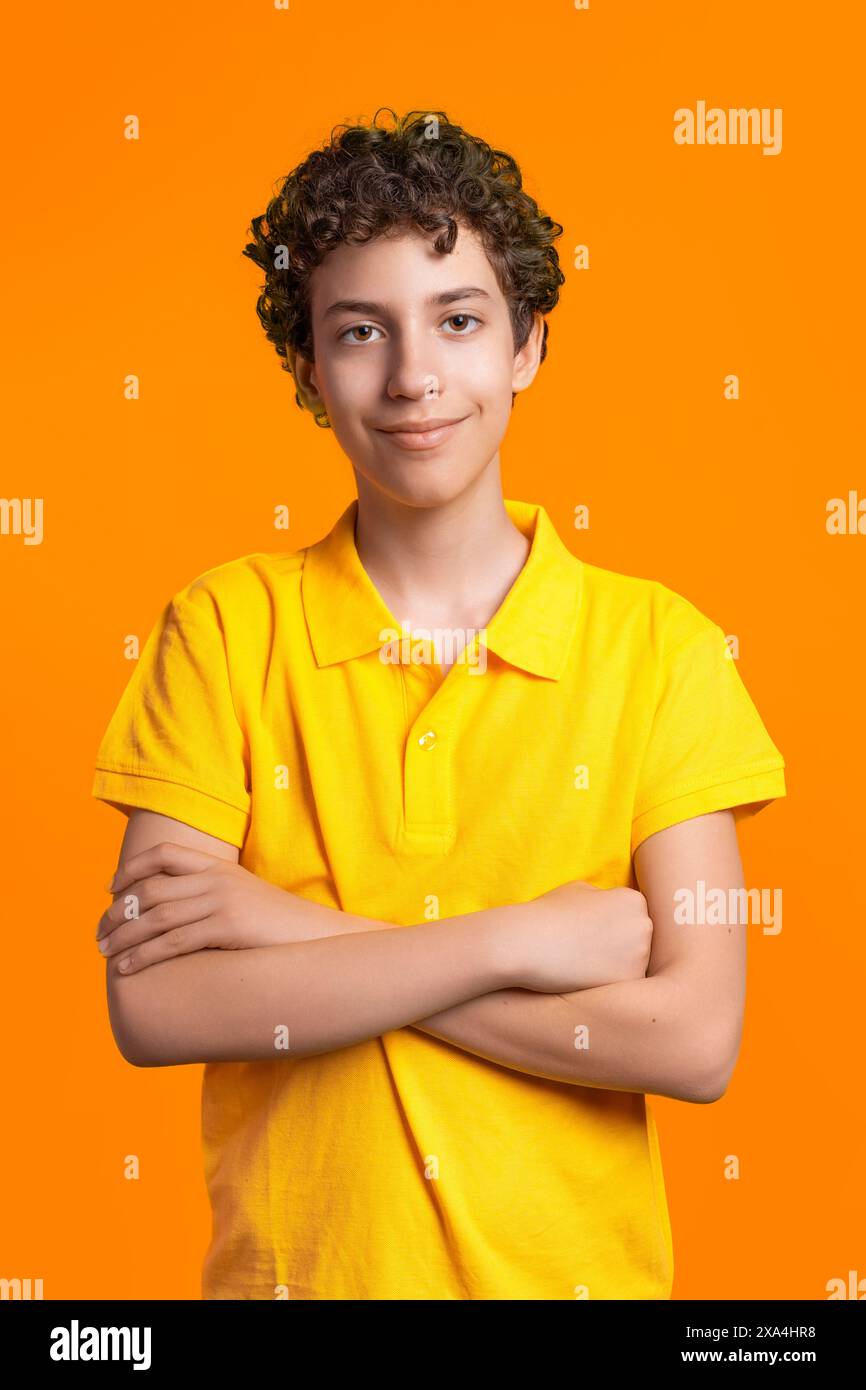 Young boy in a yellow polo shirt standing with arms crossed against an ...