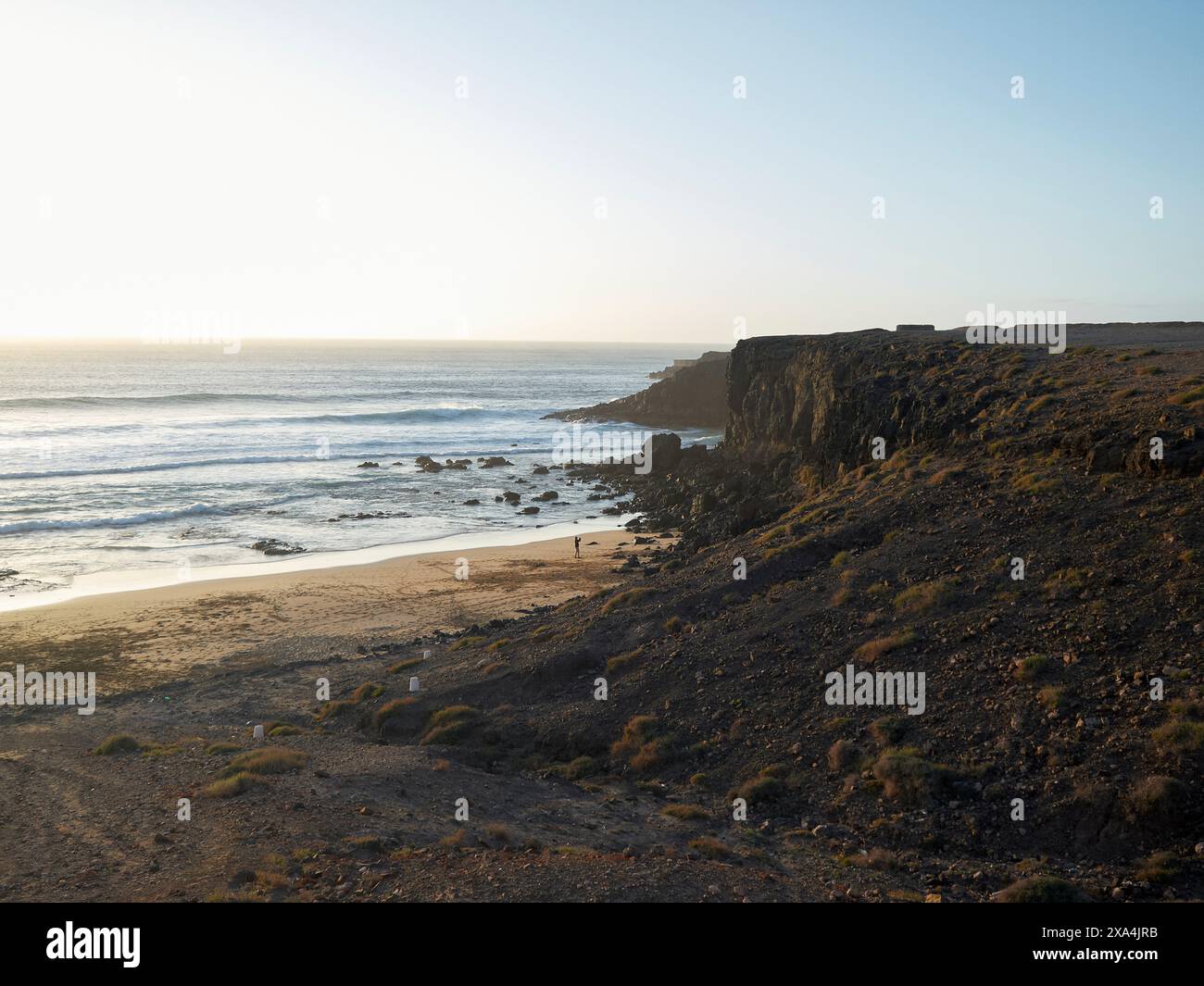 Sunrise illuminates a serene beach landscape with a rugged cliff line ...