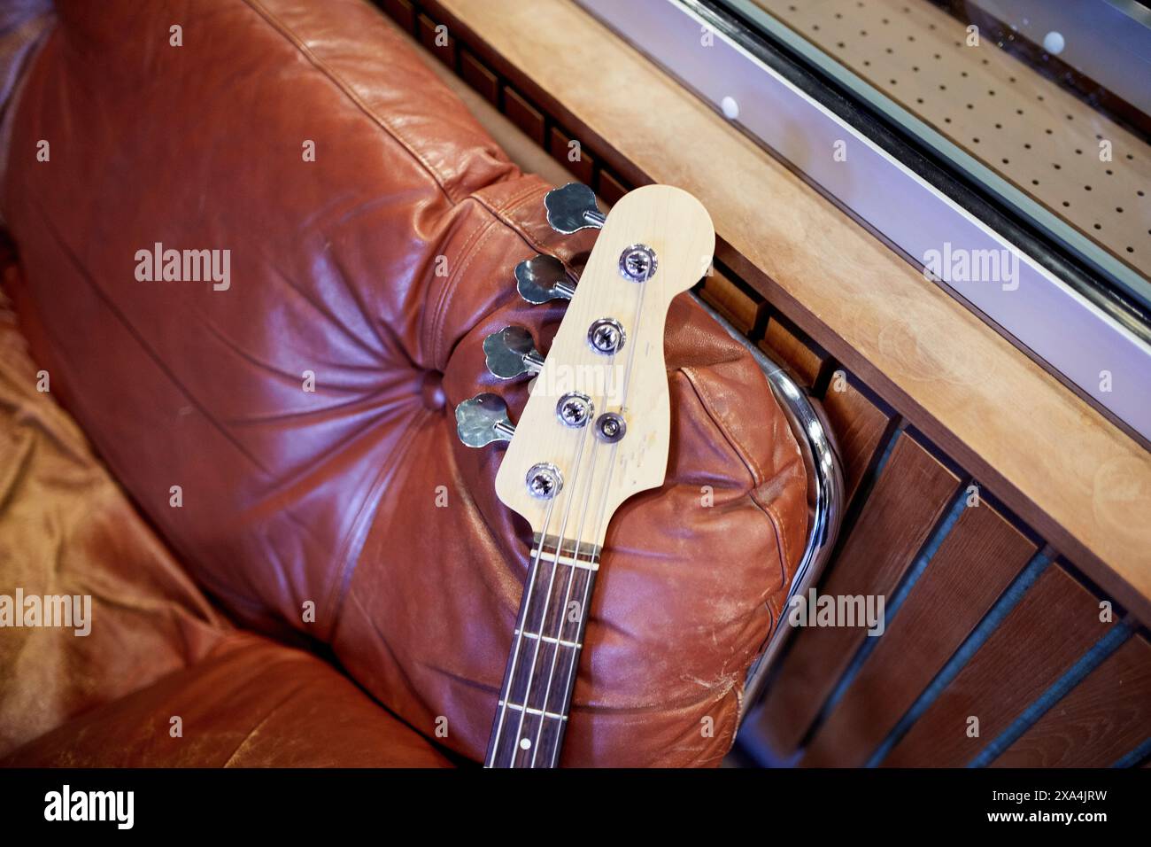 An electric bass guitar rests horizontally worn brown leather couch hi ...