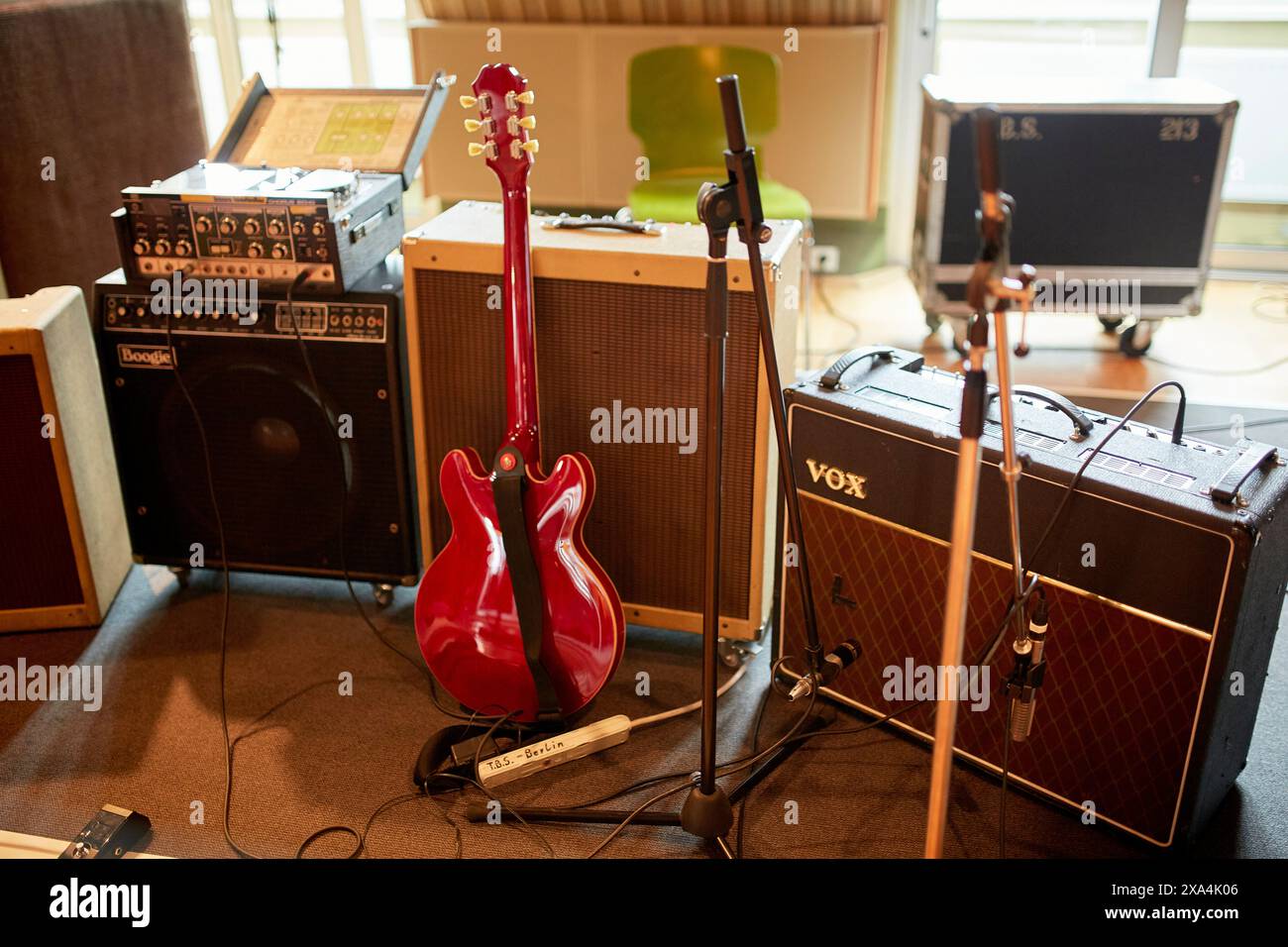 A red electric guitar stands between a microphone and a Vox amplifier ...