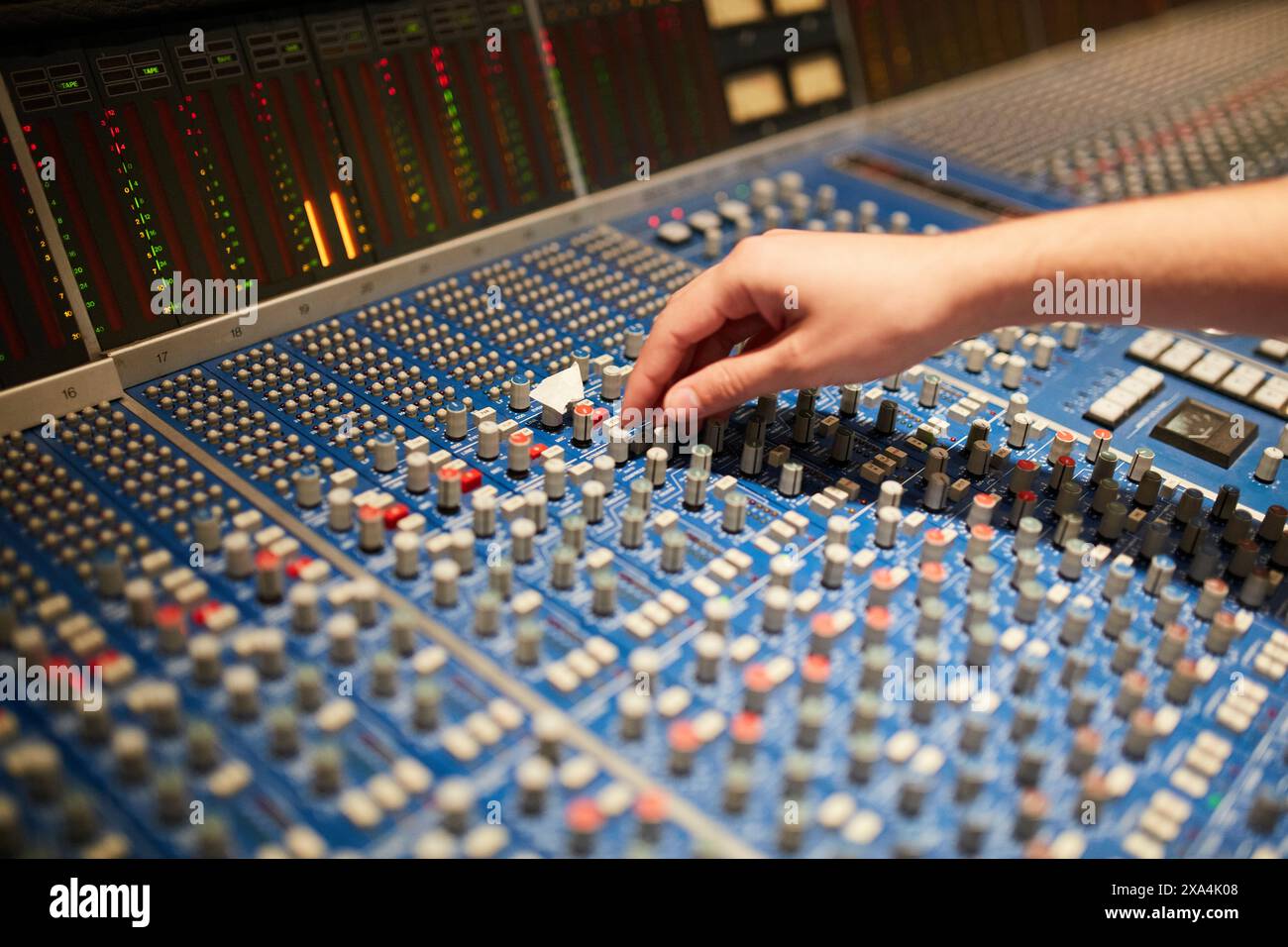 A close-up image of a hand adjusting sliders on a professional audio ...