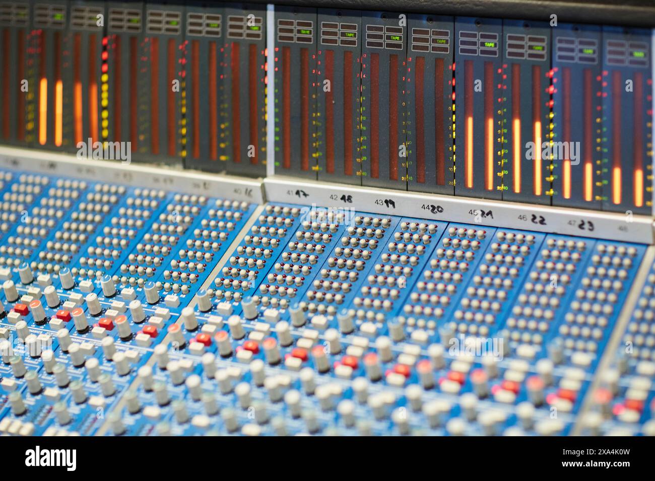 A close-up view of a professional audio mixing console with illuminated level meters displaying ...