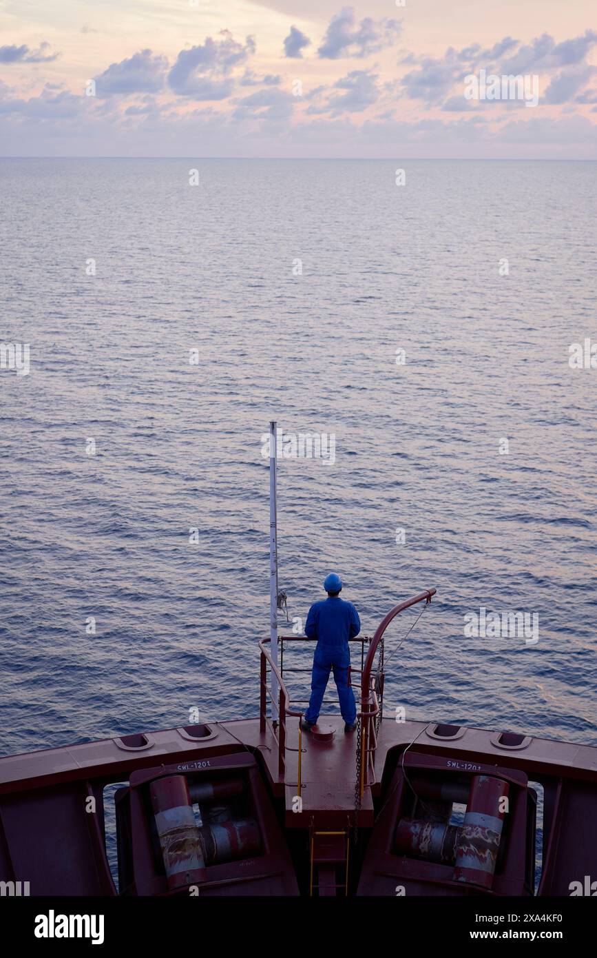 A person stands on the stern of a ship, gazing out at the vast ocean ...