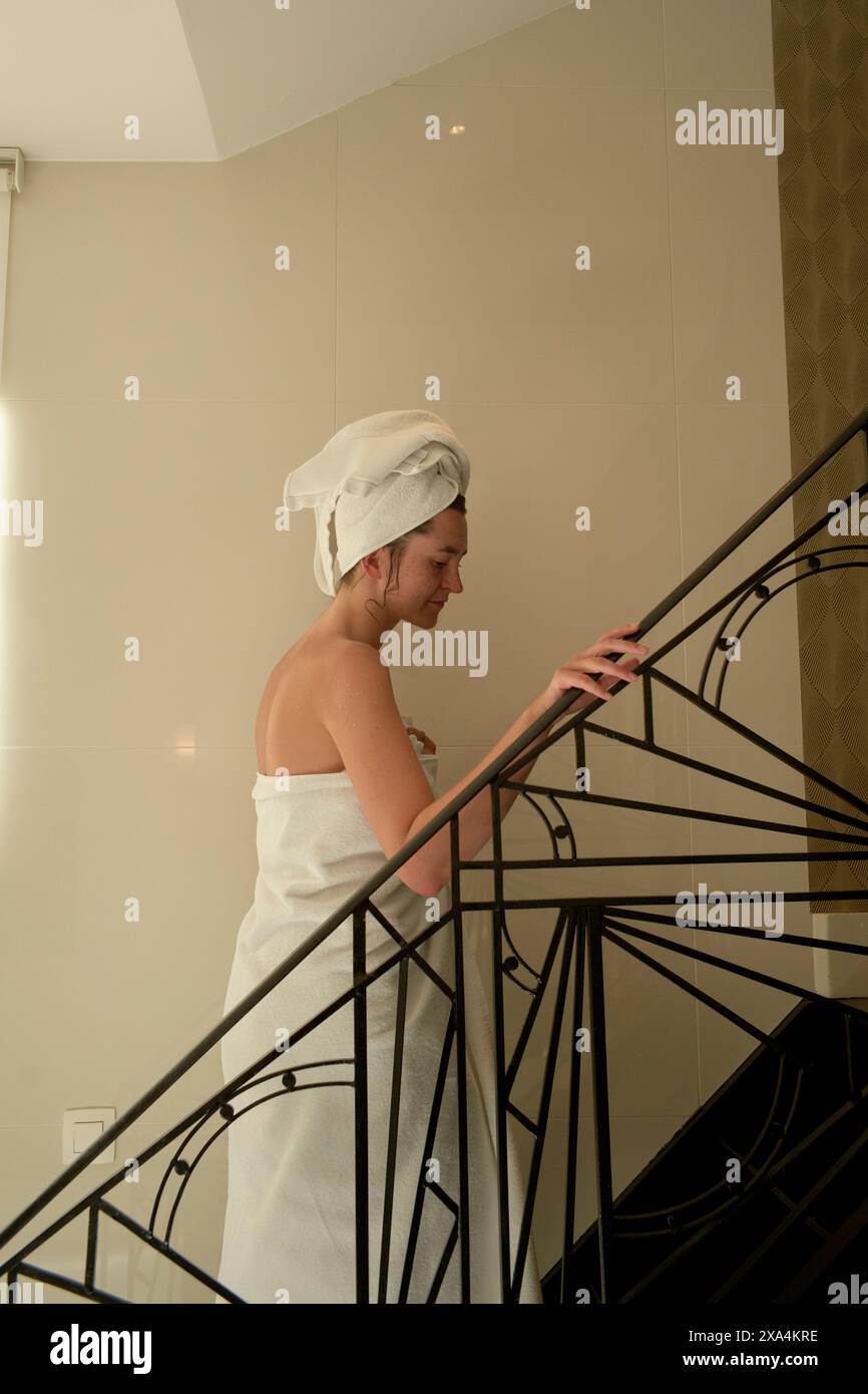 A person wrapped in a towel, with another towel on their head, is ...