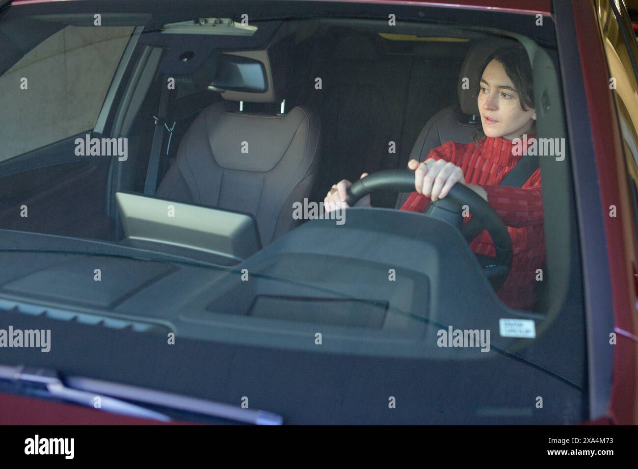 A person is sitting in the driver's seat of a red car, holding the ...