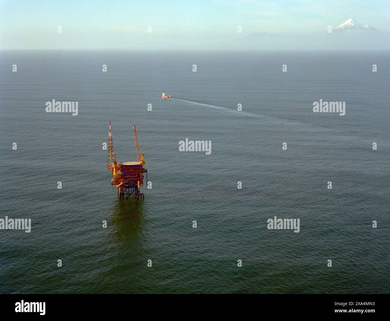 An offshore oil platform stands in the ocean with a ship sailing in the ...