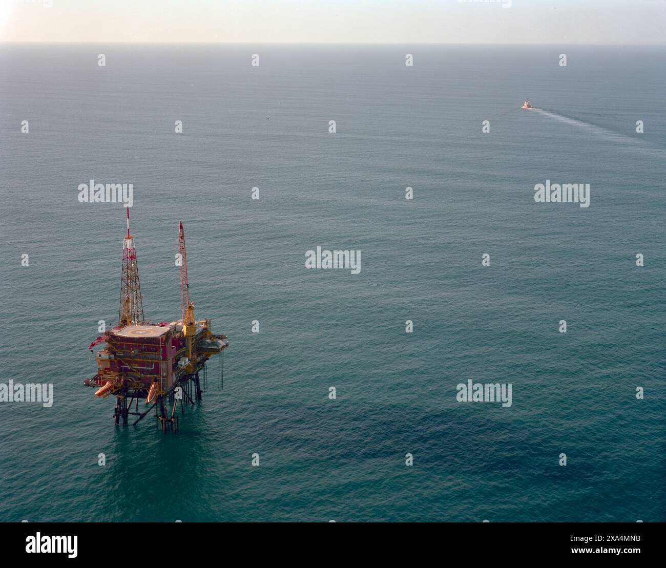 An offshore oil drilling platform stands in the midst of a calm sea ...